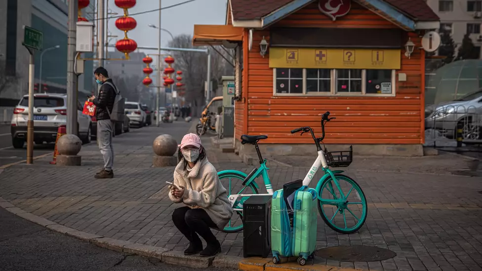 O femeie stă lângă pungi de cumpărături pe marginea unui drum din Beijing