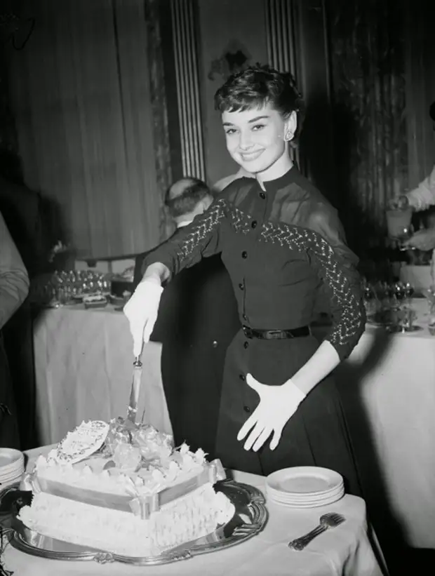 Audrey Hepburn poserer med en kake under et cocktailparty til ære for henne.