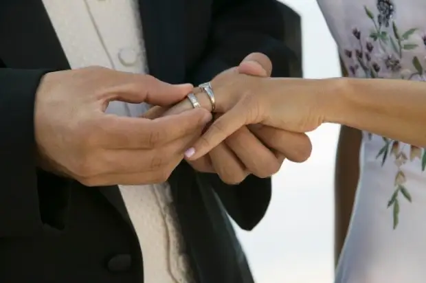 A man puts a ring on a woman's finger next to an engagement